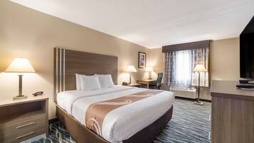 Quarto de hotel com uma cama grande, duas mesas de cabeceira com luminárias, uma escrivaninha, uma cadeira e uma televisão.