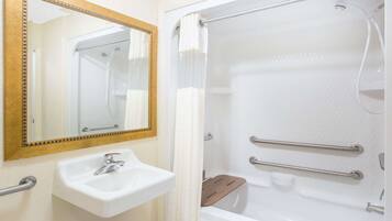 Casa de banho com lavatório branco, espelho com moldura decorativa e chuveiro com barras de apoio.