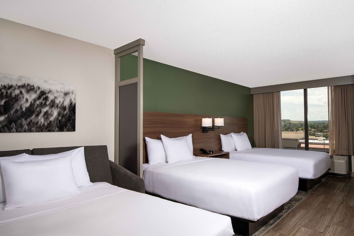 Quarto de hotel com duas camas, um quadro na parede e vista para a cidade.