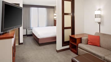 Quarto de hotel com cama, televisão, sofá, escrivaninha e abajur.