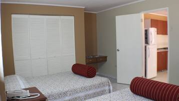 Quarto com duas camas, telefone ao lado da cama, guarda-roupa e uma kitchenette no quarto adjacente.