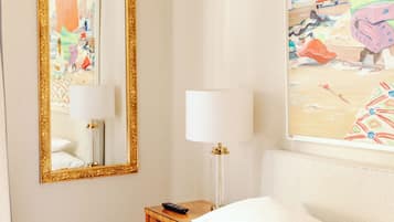 Quarto de hotel com cama, mesa de cabeceira com abajur, espelho e um quadro na parede.