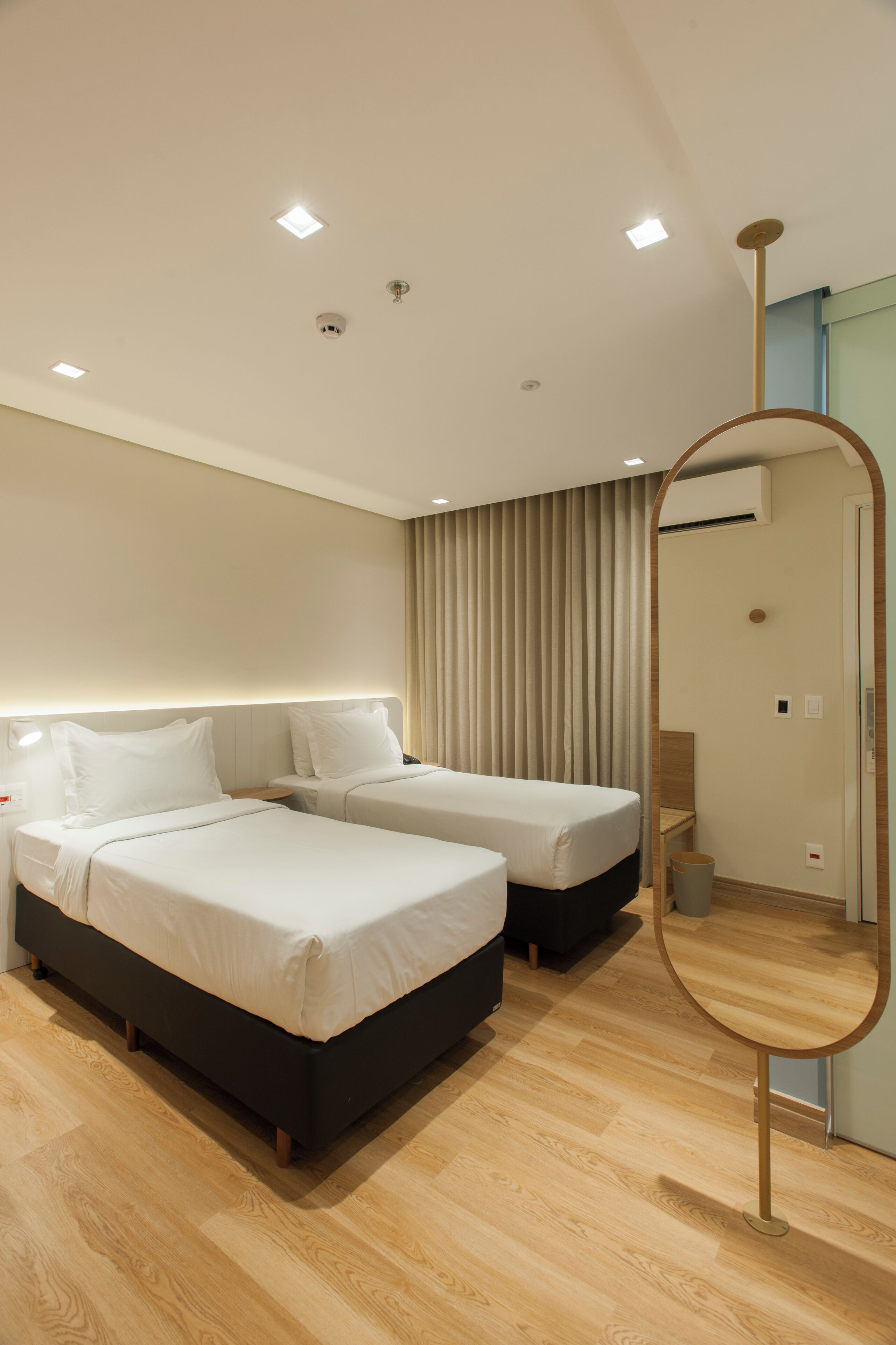 Quarto de hotel moderno com duas camas, um espelho grande e piso de madeira.