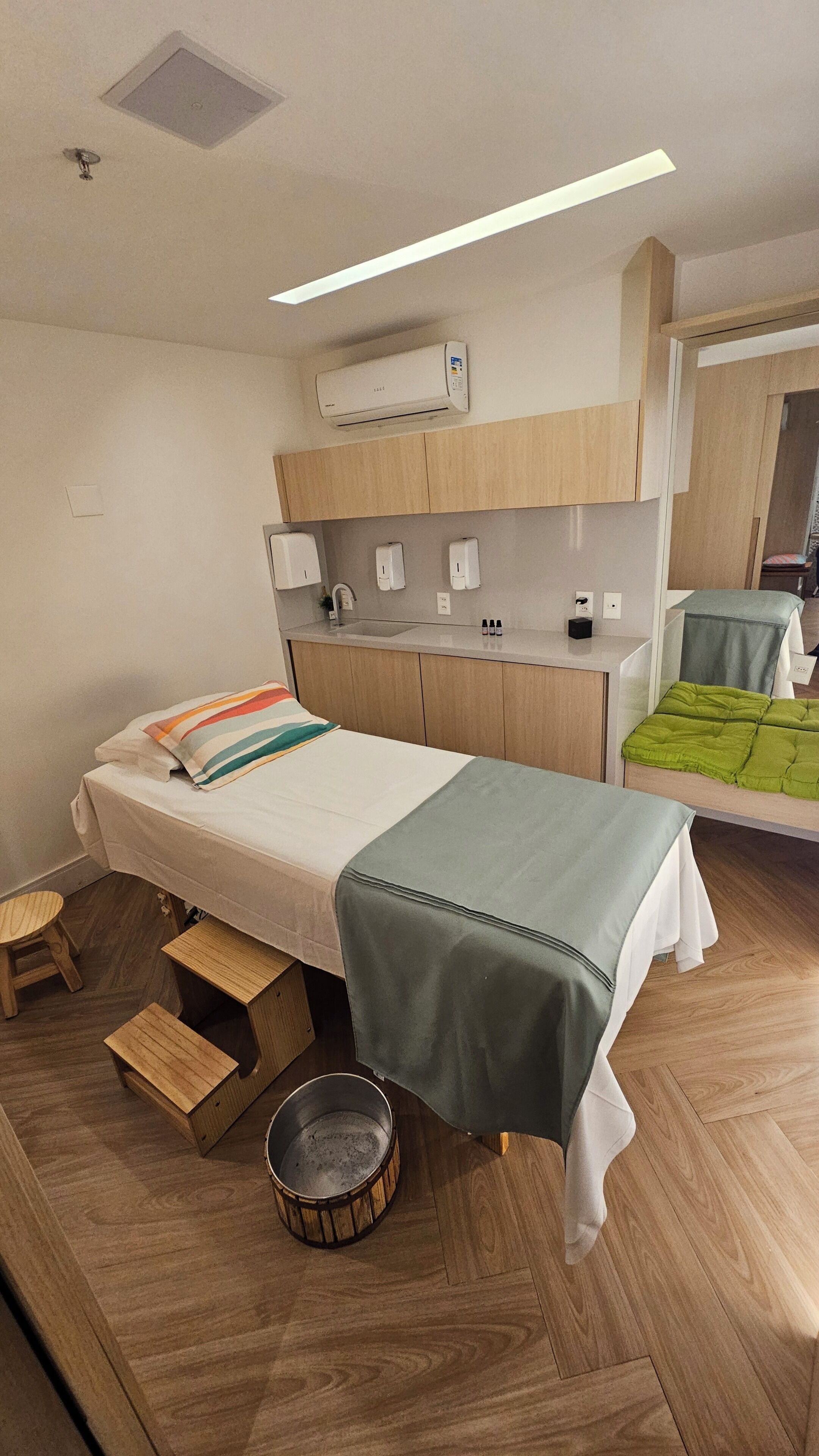 Um quarto com uma cama, um banquinho, um balde, uma pia e um espelho.