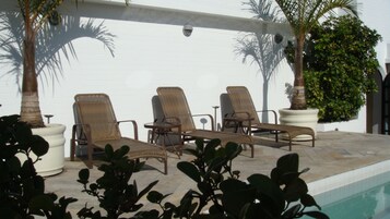 Uma área na beira da piscina com espreguiçadeiras e plantas em vasos.