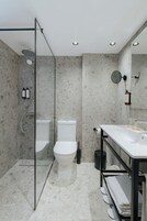 Um banheiro moderno com chuveiro em cabine de vidro, vaso sanitário branco, pia com espelho e porta-toalhas.