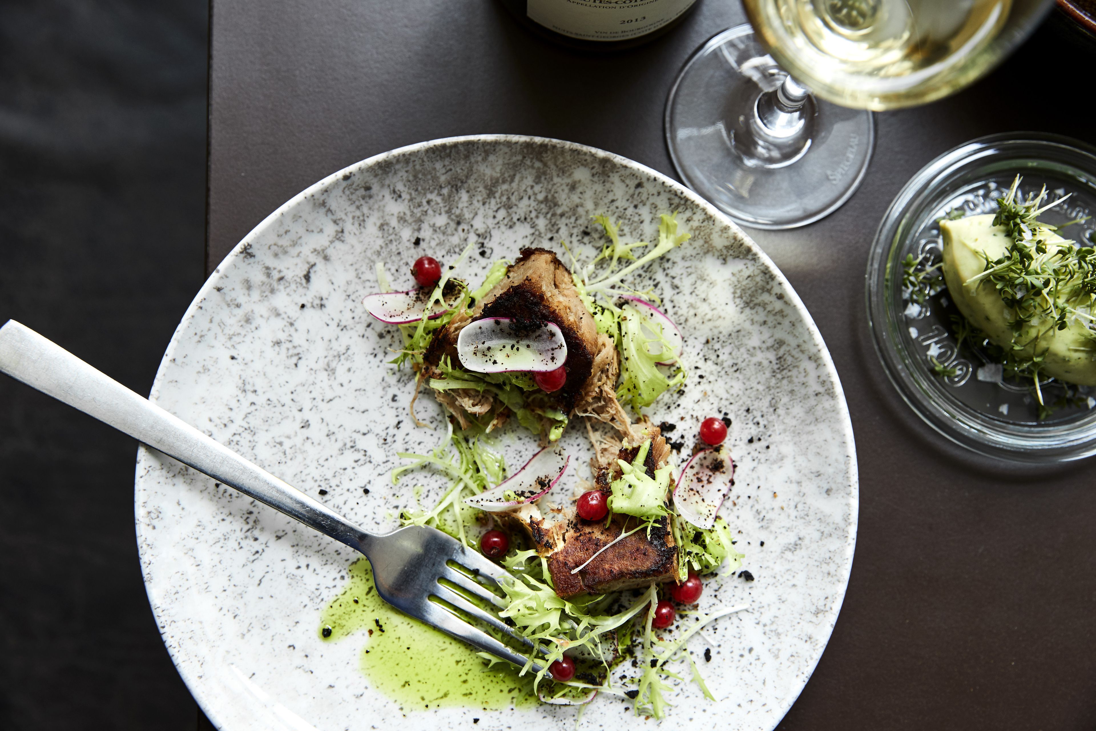 Um prato de comida com um garfo, um copo de vinho branco e uma garrafa de vinho sobre uma mesa.