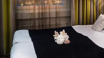 Quarto de hotel com cama, janela com cortinas e vista para a cidade à noite.