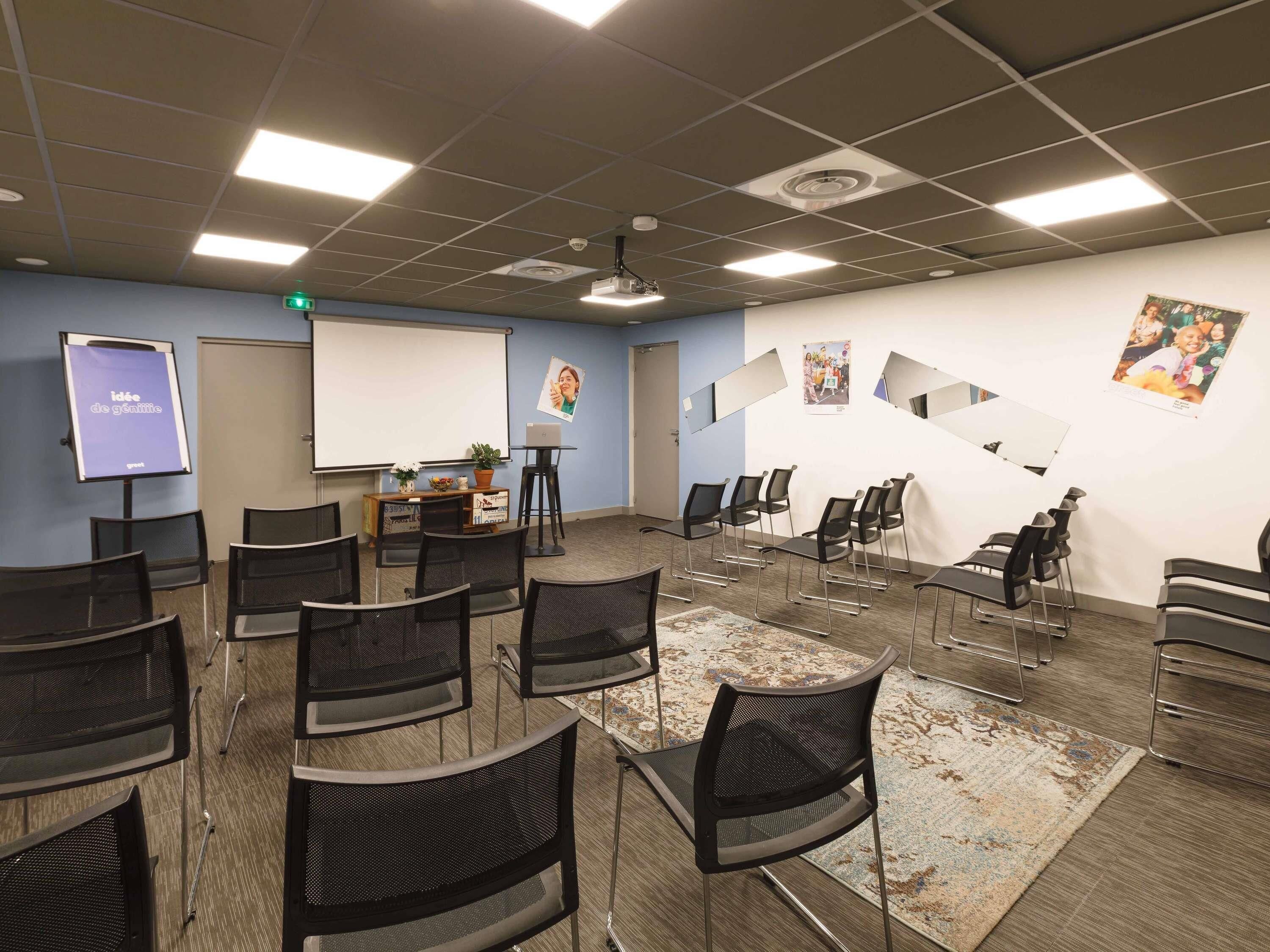 Sala de conferências com quadro branco, projetor e disposição de assentos para apresentações.