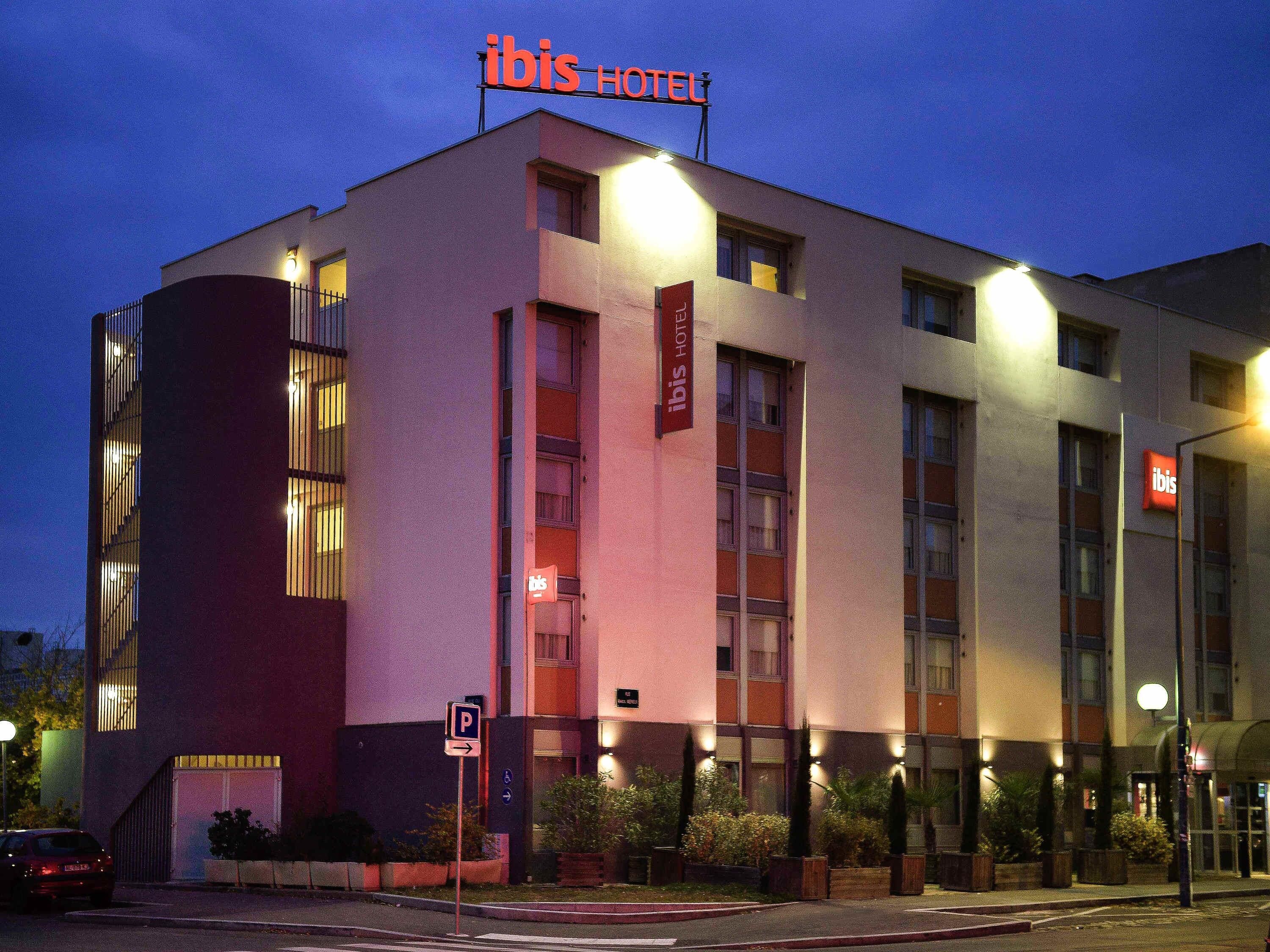 Um edifício de hotel moderno com um destaque para o letreiro 'ibis HOTEL' no topo.