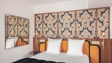 Quarto de hotel com uma cama grande, cabeceira com padrão decorativo, mesa de cabeceira com abajur e espelho na parede.