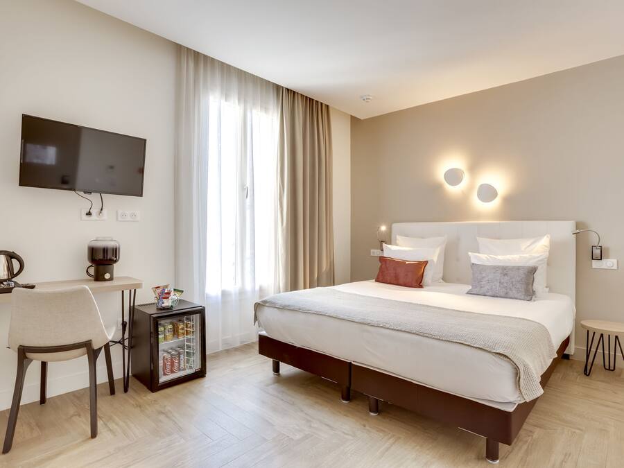 Quarto de hotel moderno com cama, escrivaninha com cadeira, televisão e minibar.