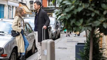 Um homem com uma mala na calçada, ao lado de carros estacionados.