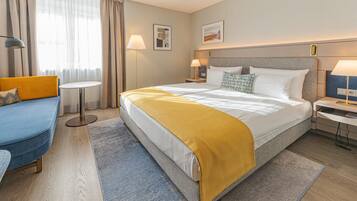 Quarto de hotel com cama, sofá, mesinha e abajur.