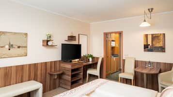 Quarto de hotel com cama, escrivaninha com televisão, cadeira, mesinha e espelho.