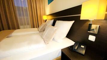 Quarto de hotel com cama, duas luminárias de cabeceira, mesa de cabeceira com telefone e janela com cortinas.