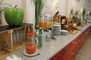 Um buffet de café da manhã com uma maçã verde grande, dispensadores de suco e diversos alimentos.