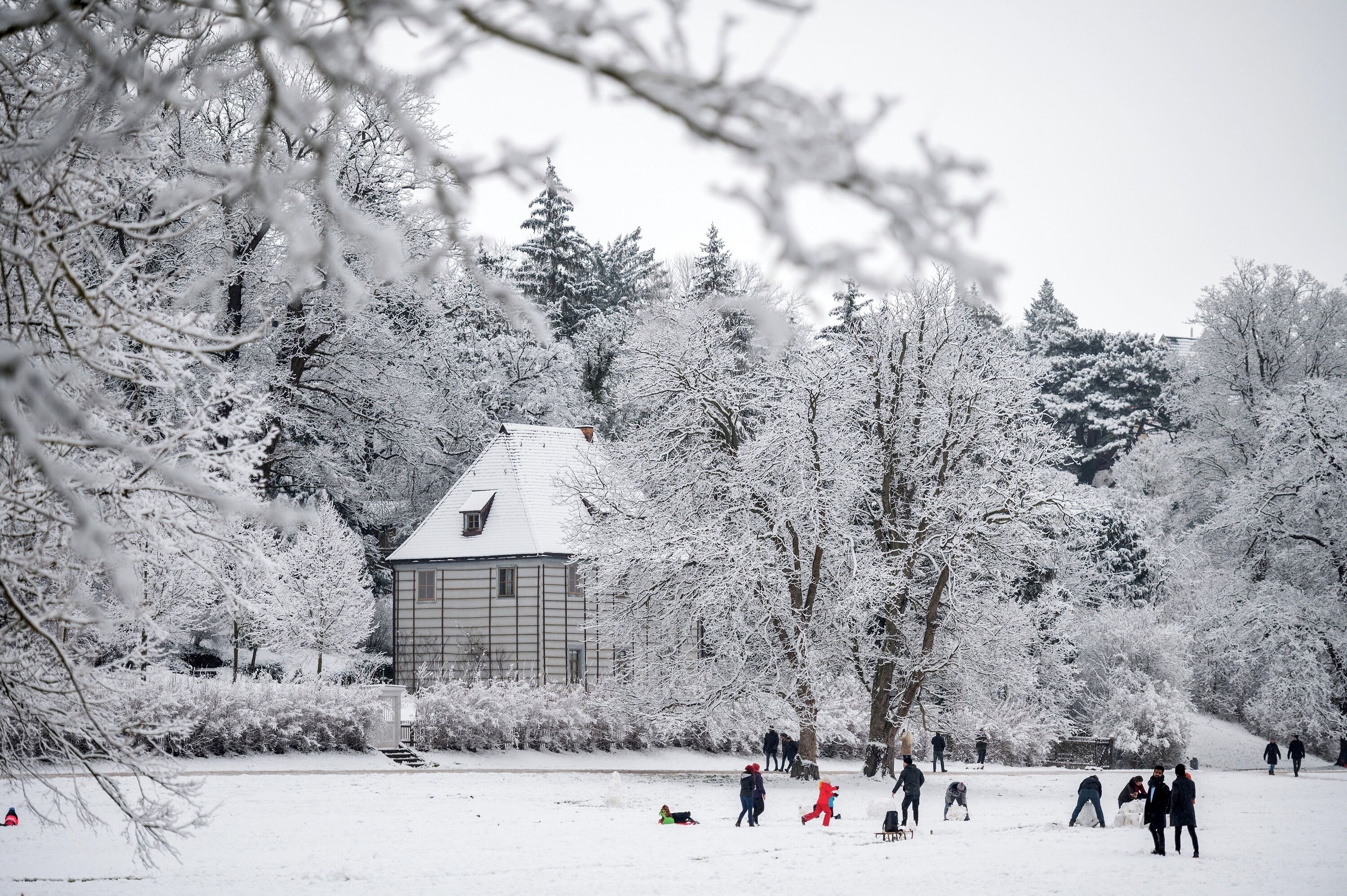 Parque coberto de neve, com um edifício e pessoas praticando atividades de inverno.