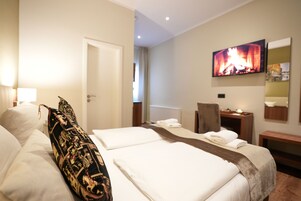 Quarto de hotel com cama, televisão, espelho e mesa de cabeceira com abajur.