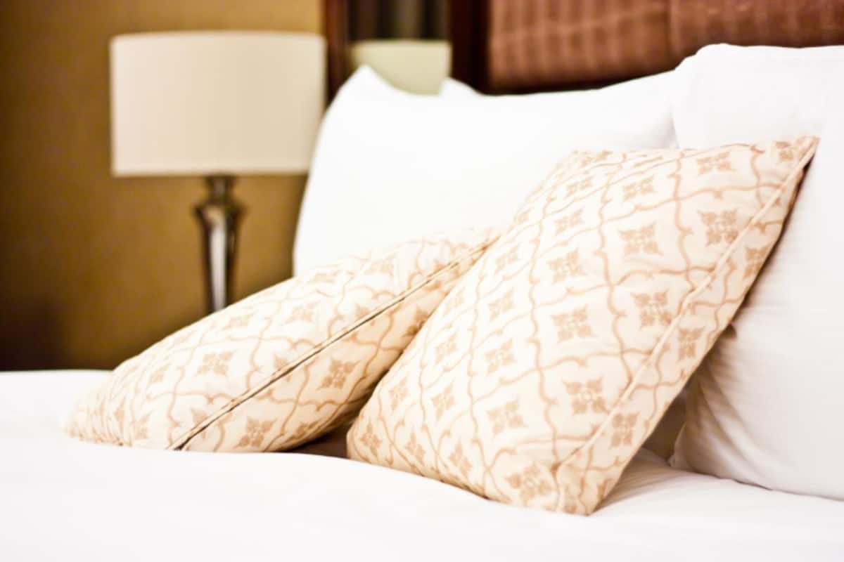 Uma cama com duas almofadas estampadas e uma luminária ao fundo.