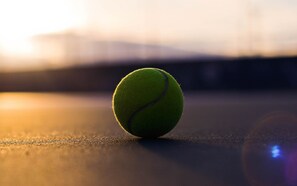 Uma bola de tênis em uma superfície lisa, com fundo desfocado.