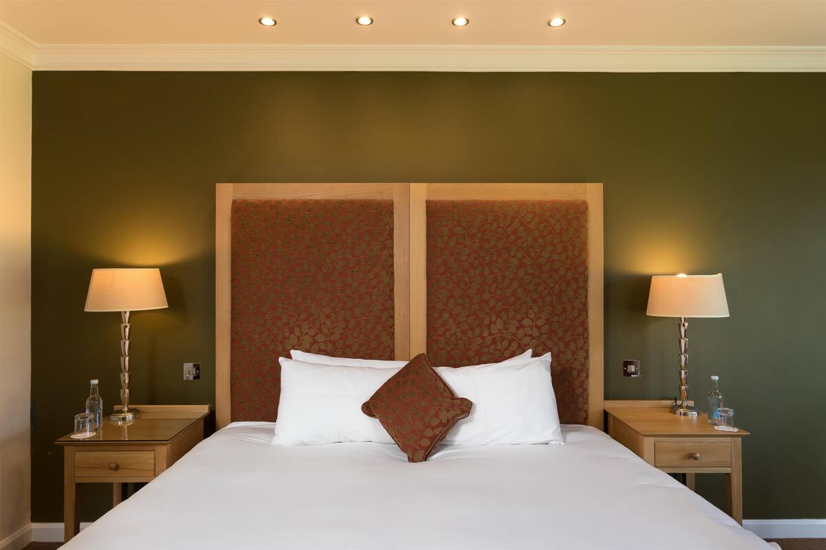 Quarto de hotel com uma cama grande, duas mesas de cabeceira e cabeceira com design estampado.