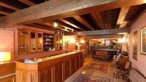 Um quarto acolhedor e bem iluminado, com um bar de madeira, estantes de livros e um espaço de estar com um tapete estampado.