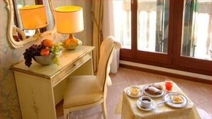 Quarto com escrivaninha de madeira, uma cadeira, mesa com itens de café da manhã e janela com cortinas.
