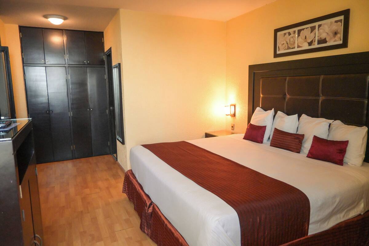 Quarto de hotel com uma cama grande, um guarda-roupa, uma escrivaninha e um candeeiro fixo na parede.