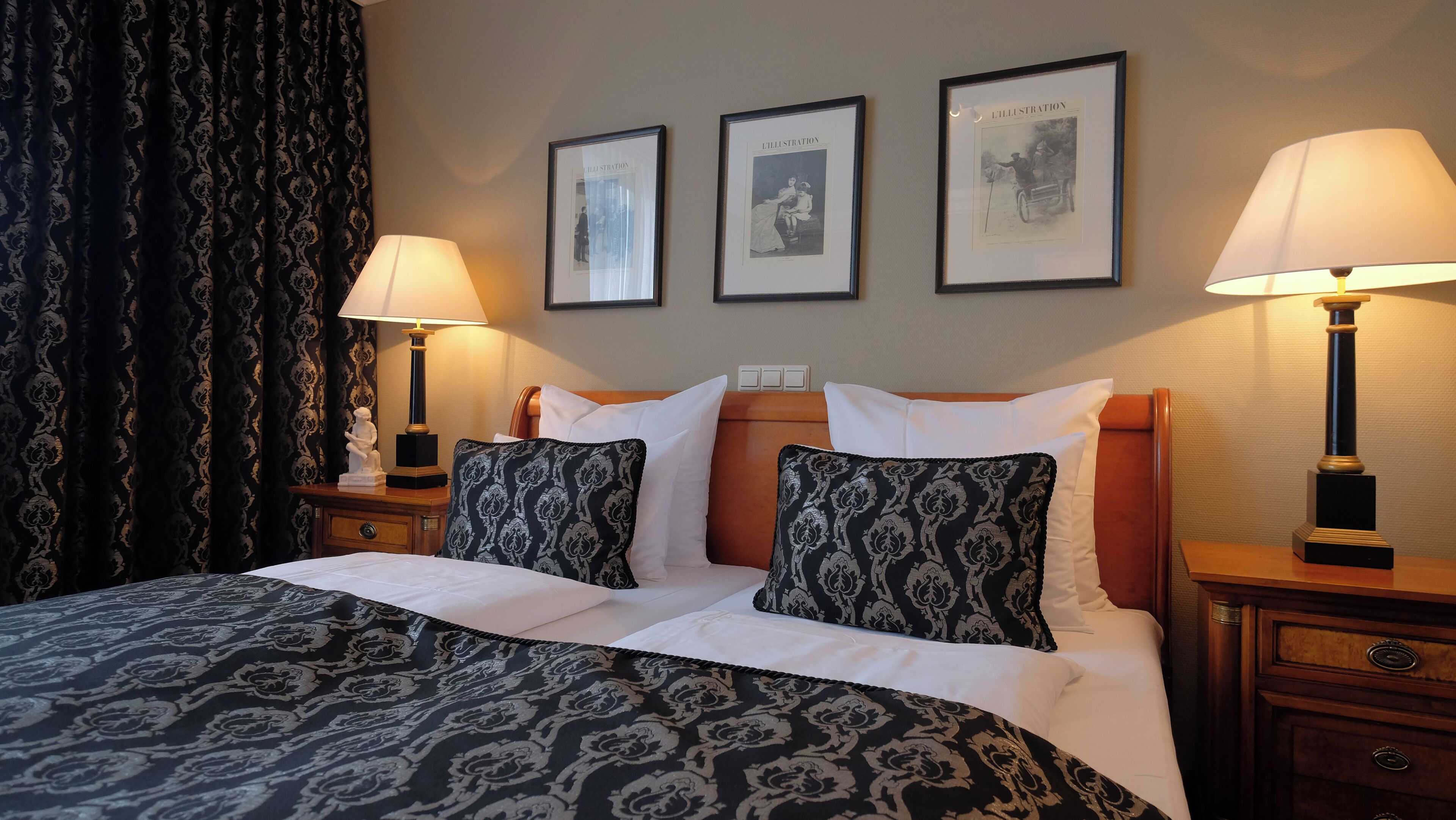 Uma cama bem arrumada com roupa de cama estampada, duas luminárias de cabeceira e três quadros na parede.