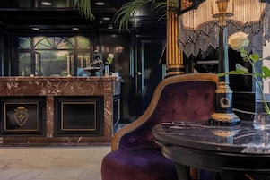 Um saguão com uma recepção de mármore, uma poltrona roxa, uma mesa redonda com um vaso e um lustre.