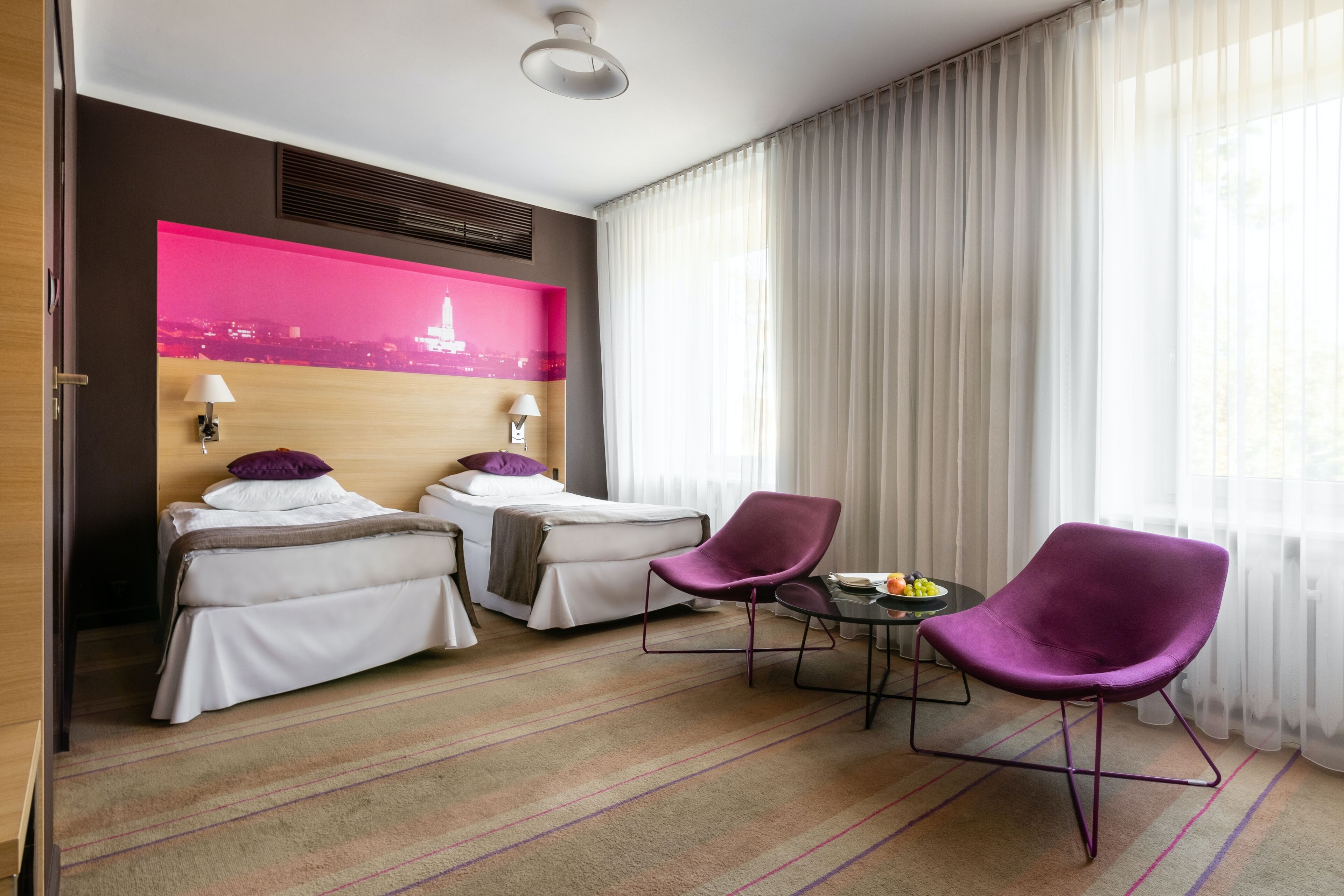 Quarto de hotel com duas camas, uma mesa de jantar e cadeiras roxas.