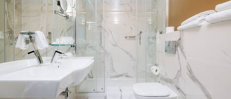 Uma casa de banho moderna com chuveiro envolto em vidro, lavatório branco e sanita.