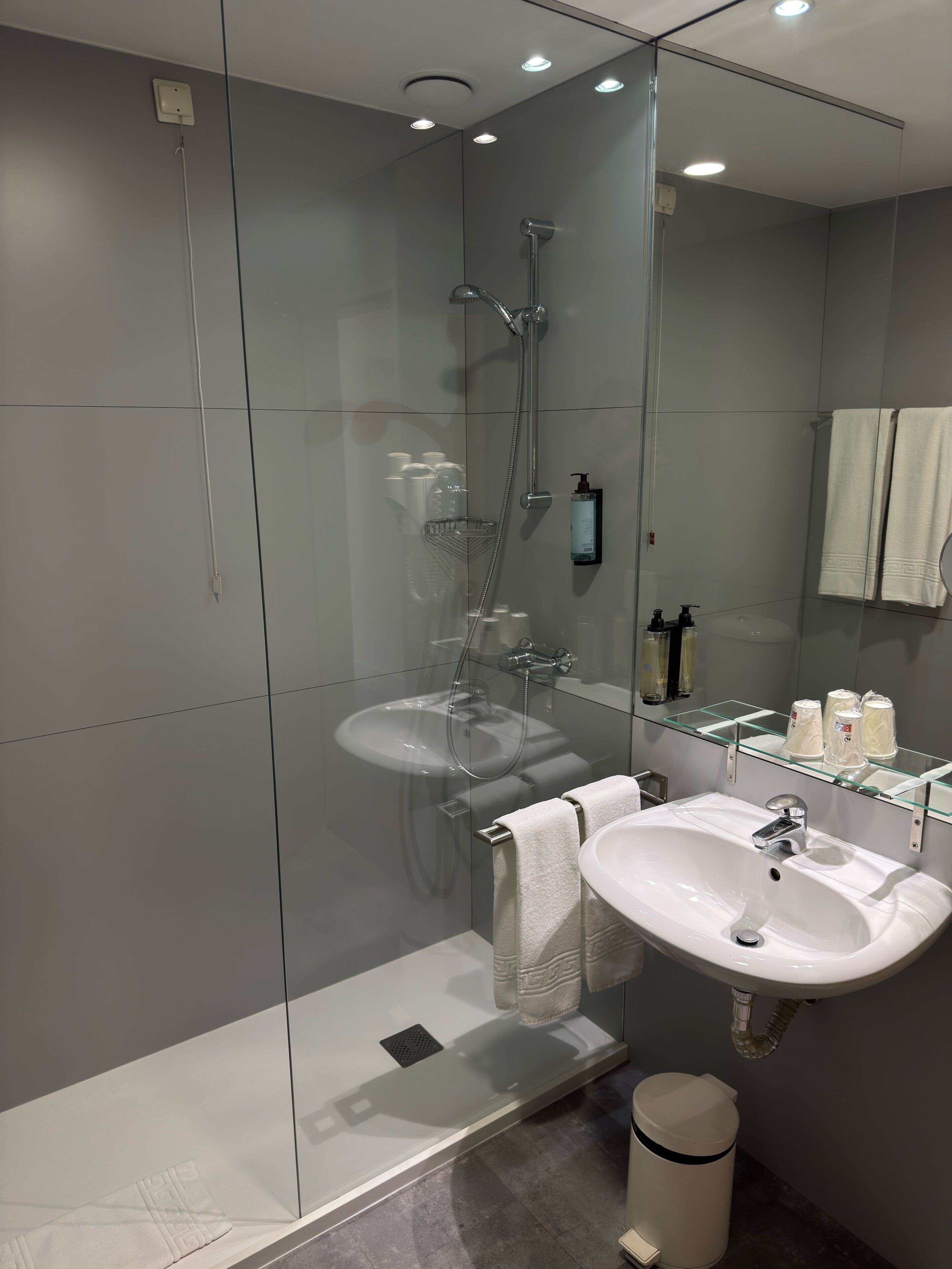 Uma casa de banho moderna com chuveiro envidraçado, lavatório branco e espelho sobre o lavatório.