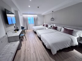 Quarto de hotel moderno com duas camas, uma escrivaninha, uma cadeira, uma televisão e uma janela com cortinas.