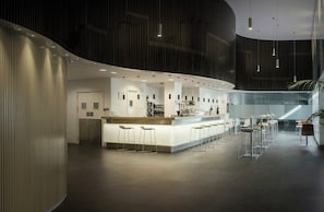 Uma área de bar moderna com balcão curvo, banquetas e iluminação pendente.