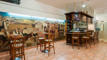 Uma área de bar com cadeiras e mesas de madeira, um mural na parede e um balcão com garrafas.