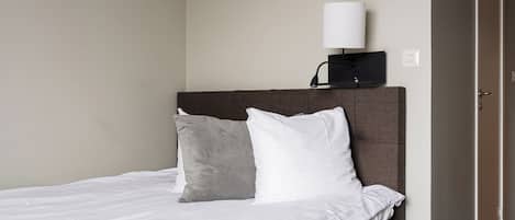 Uma cama de solteiro com roupa de cama branca, um travesseiro cinzento e uma luminária de cabeceira.