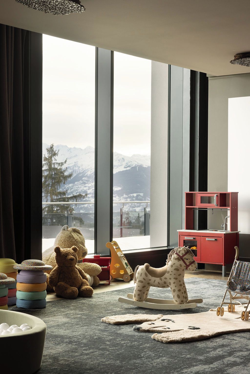 Um quarto de brincar infantil com uma janela grande, uma cozinha de brinquedo vermelha e um urso de pelúcia.