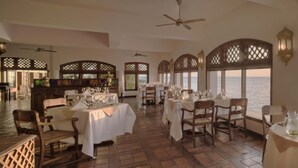 Restaurante com mesas preparadas para refeições, grandes janelas com vista para o mar e molduras de janelas de madeira tradicional.