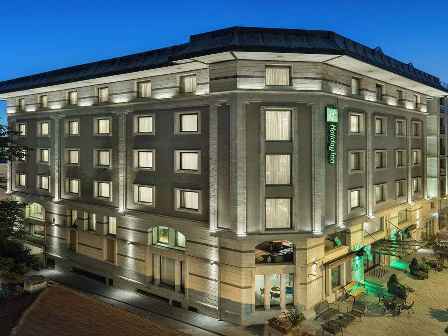 Hotel de vários andares com design moderno, apresentando uma área de varanda espaçosa com assentos e vegetação.