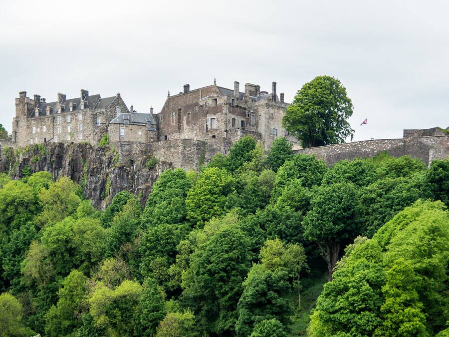 Um castelo histórico numa colina, rodeado por uma floresta densa.
