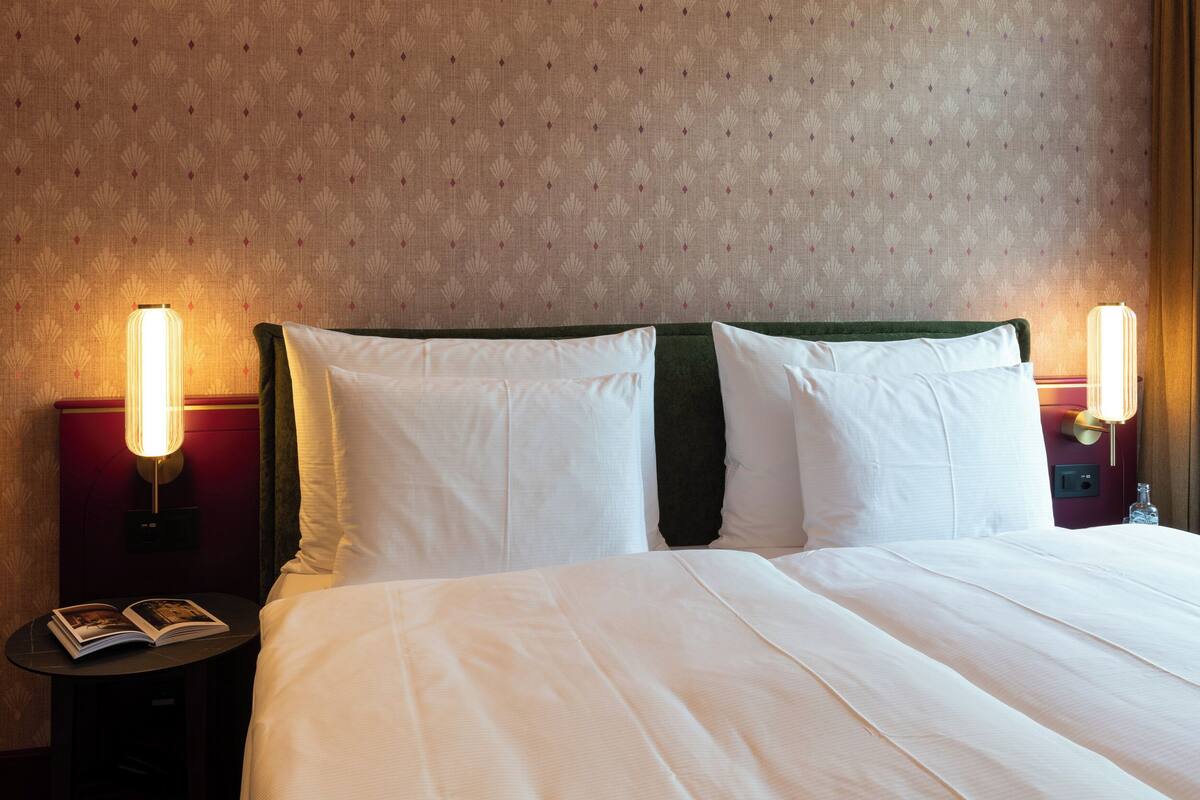 Cama bem arrumada com lençóis brancos e duas luminárias de cabeceira.