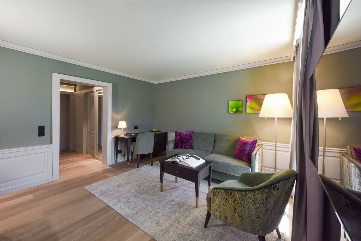 Uma sala de estar com sofá, poltrona, mesa de centro e escrivaninha com abajur.