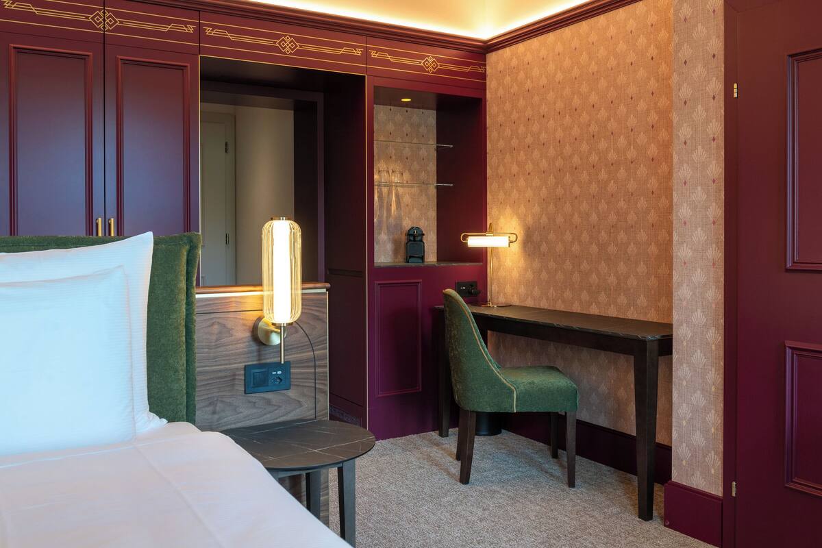Quarto de hotel com cama, escrivaninha, cadeira, espelho e guarda-roupa.