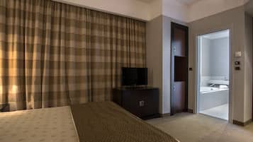 Quarto de hotel com uma cama, televisão sobre uma cômoda e banheiro visível através de uma porta aberta.