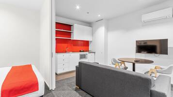 Quarto de hotel moderno com cozinha compacta, sofá, mesa de jantar e TV.