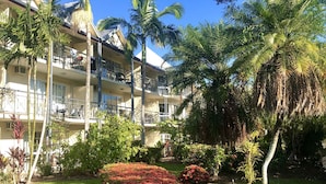 Hotel de vários andares com varandas, cercado por vegetação exuberante e plantas floridas vermelhas.