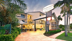 Um hotel com vários andares, área de estar ao ar livre e placa indicando acomodação com cozinha e preços acessíveis.