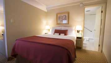 Quarto de hotel com uma cama grande, duas luminárias de cabeceira, um quadro pendurado na parede e uma porta para o banheiro.
